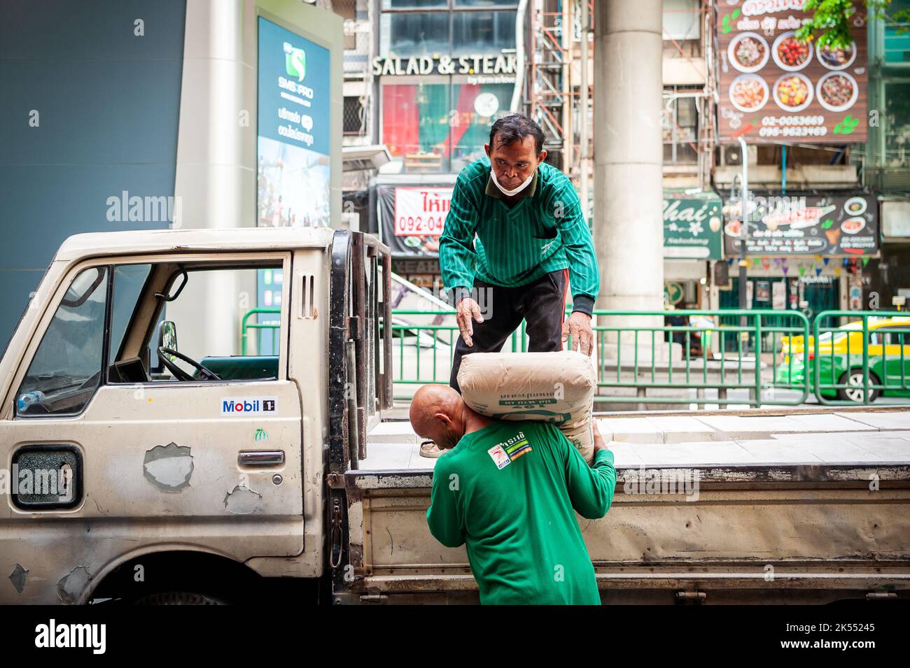 Thai construction workers unload cement or gravel from the back of a ...