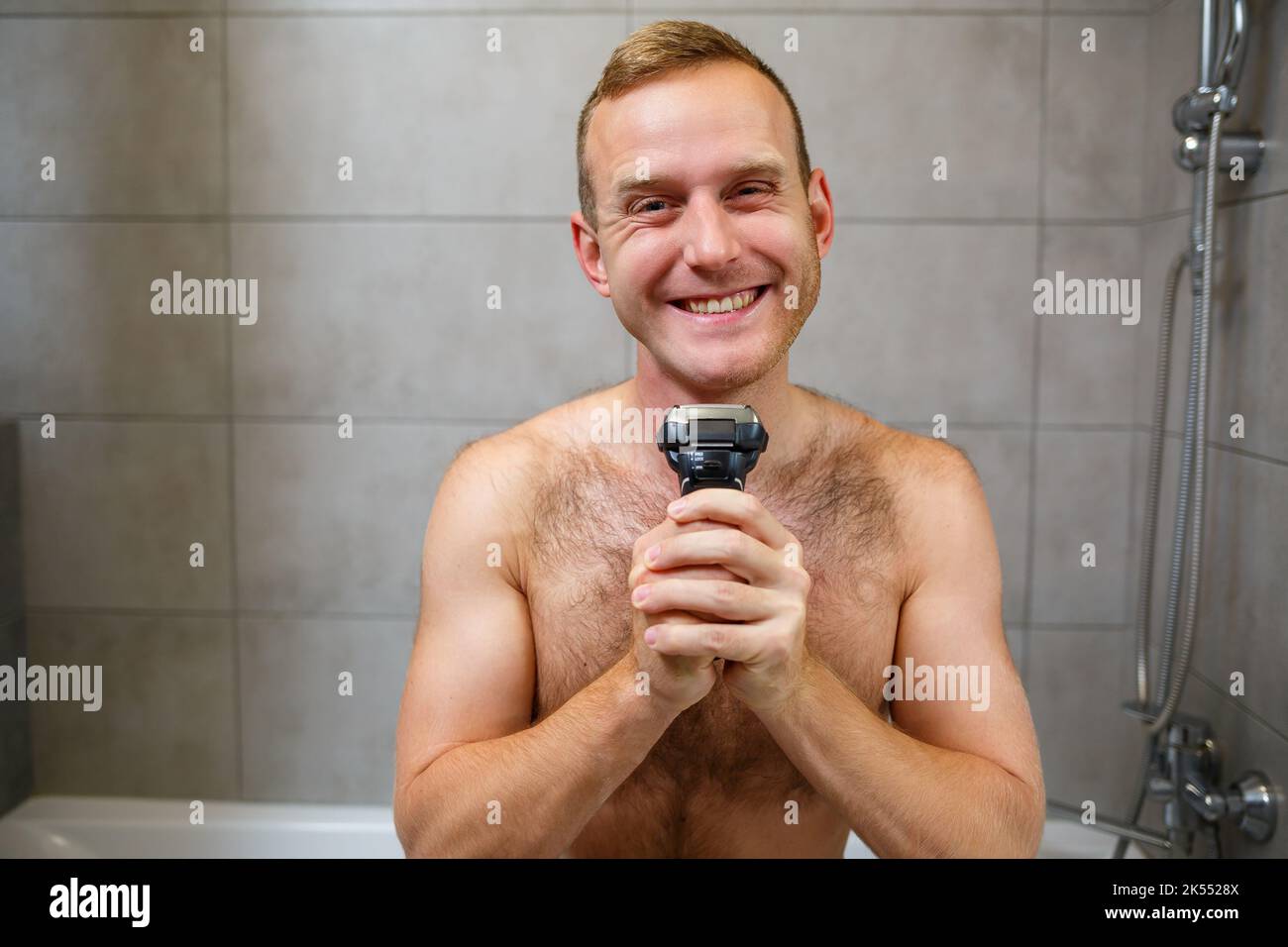 A man shaves his face with an electric razor in front of a mirror. Skin ...