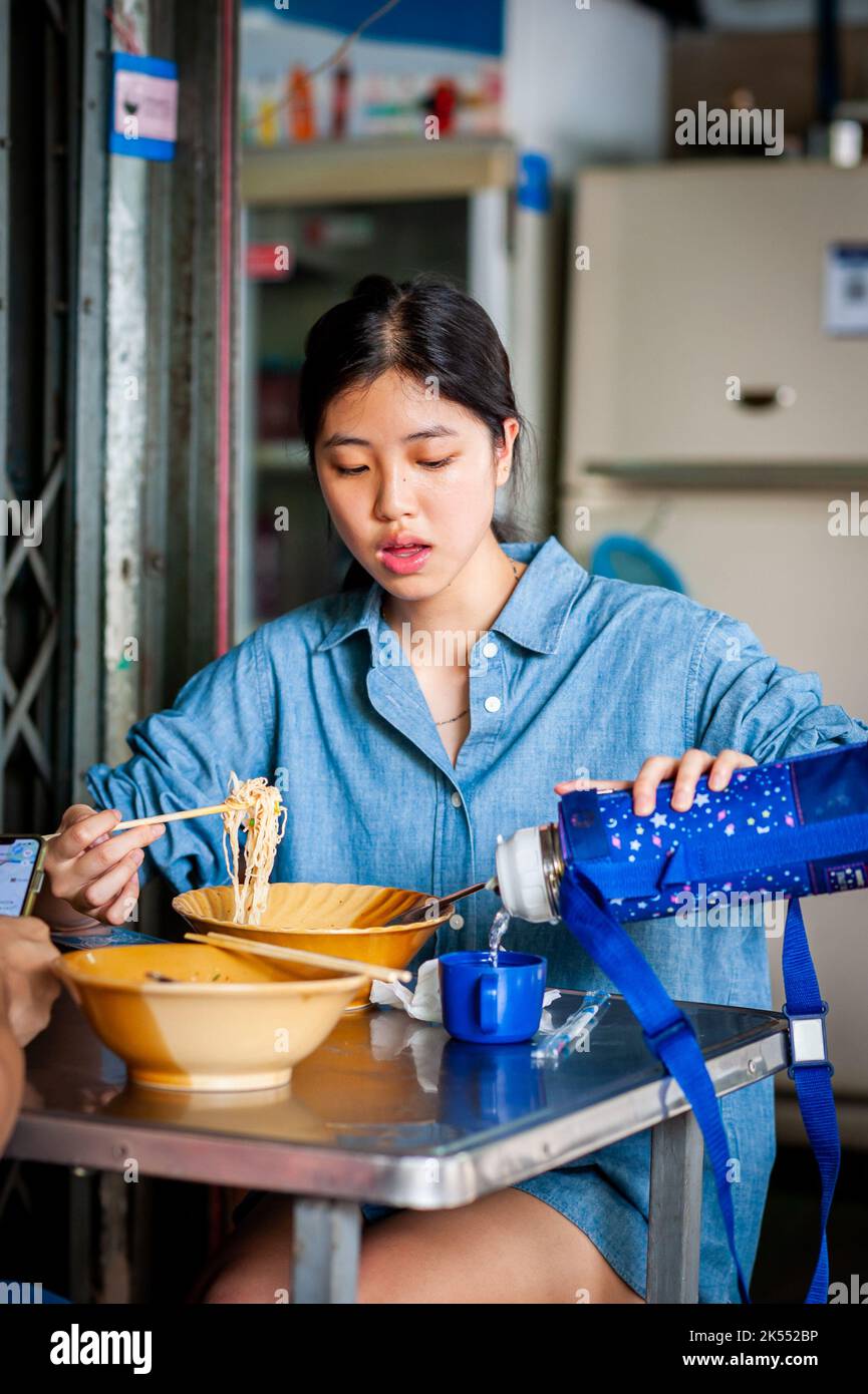 A Young Thai Girl Enjoys Some Noodle Soup In A Street Restaurant In Soi