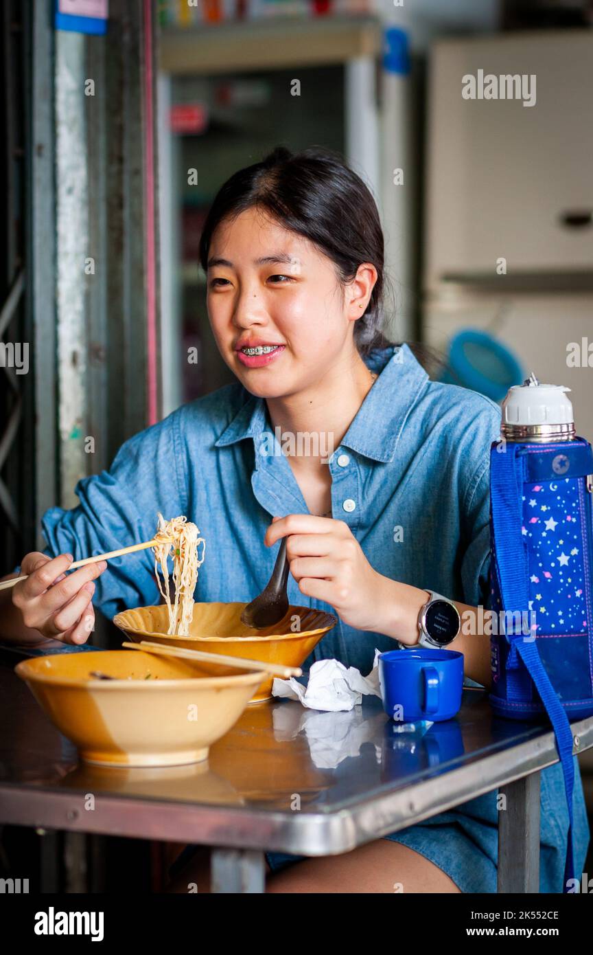A Young Thai Girl Enjoys Some Noodle Soup In A Street Restaurant In Soi Ruamrudee Bangkok