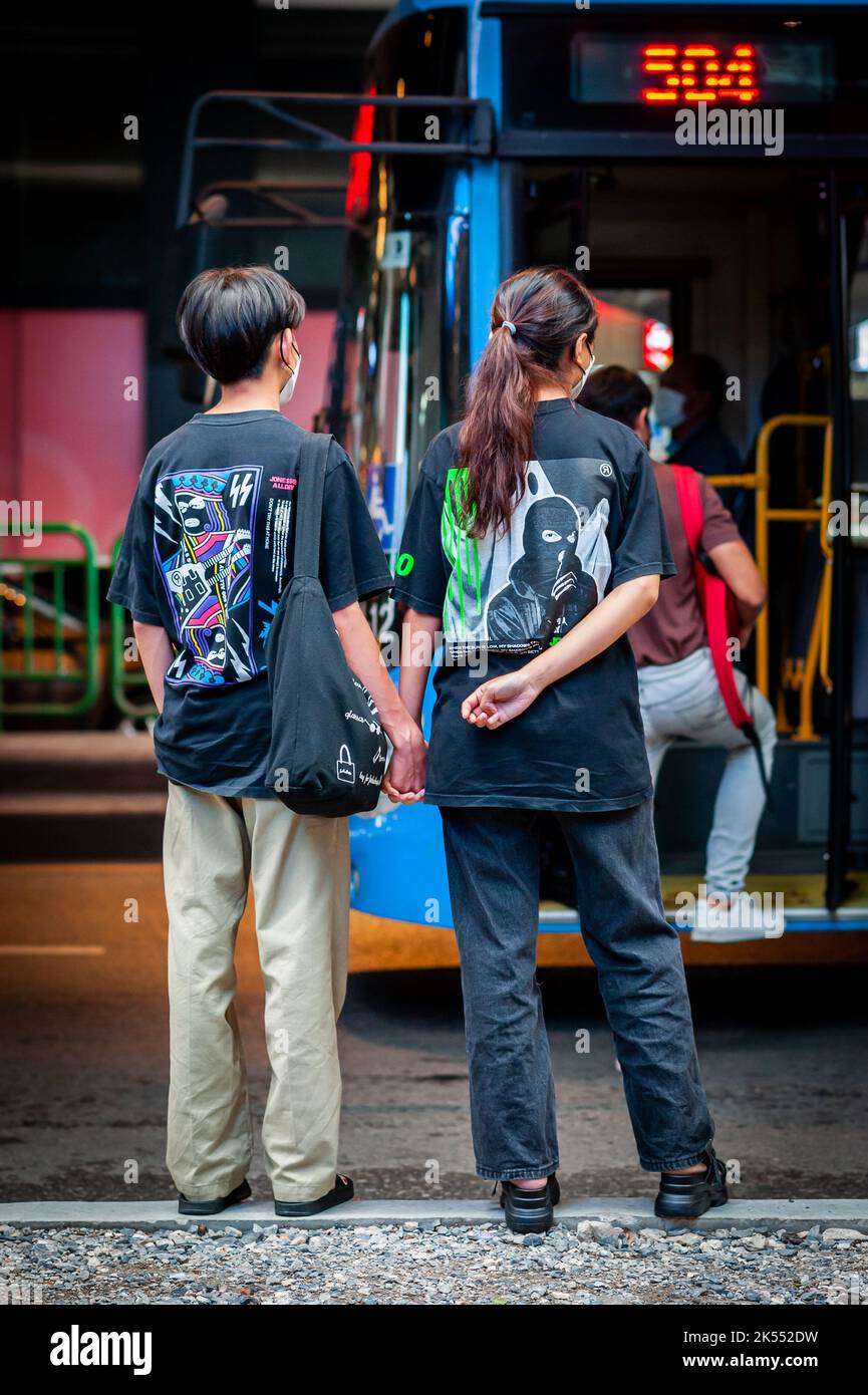 A young Thai couple hold hands and wait for their bus at Sala Daeng in ...