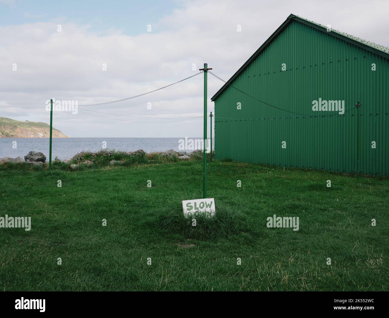 An odd empty washing line and green hut on green grass with a slow sign ...
