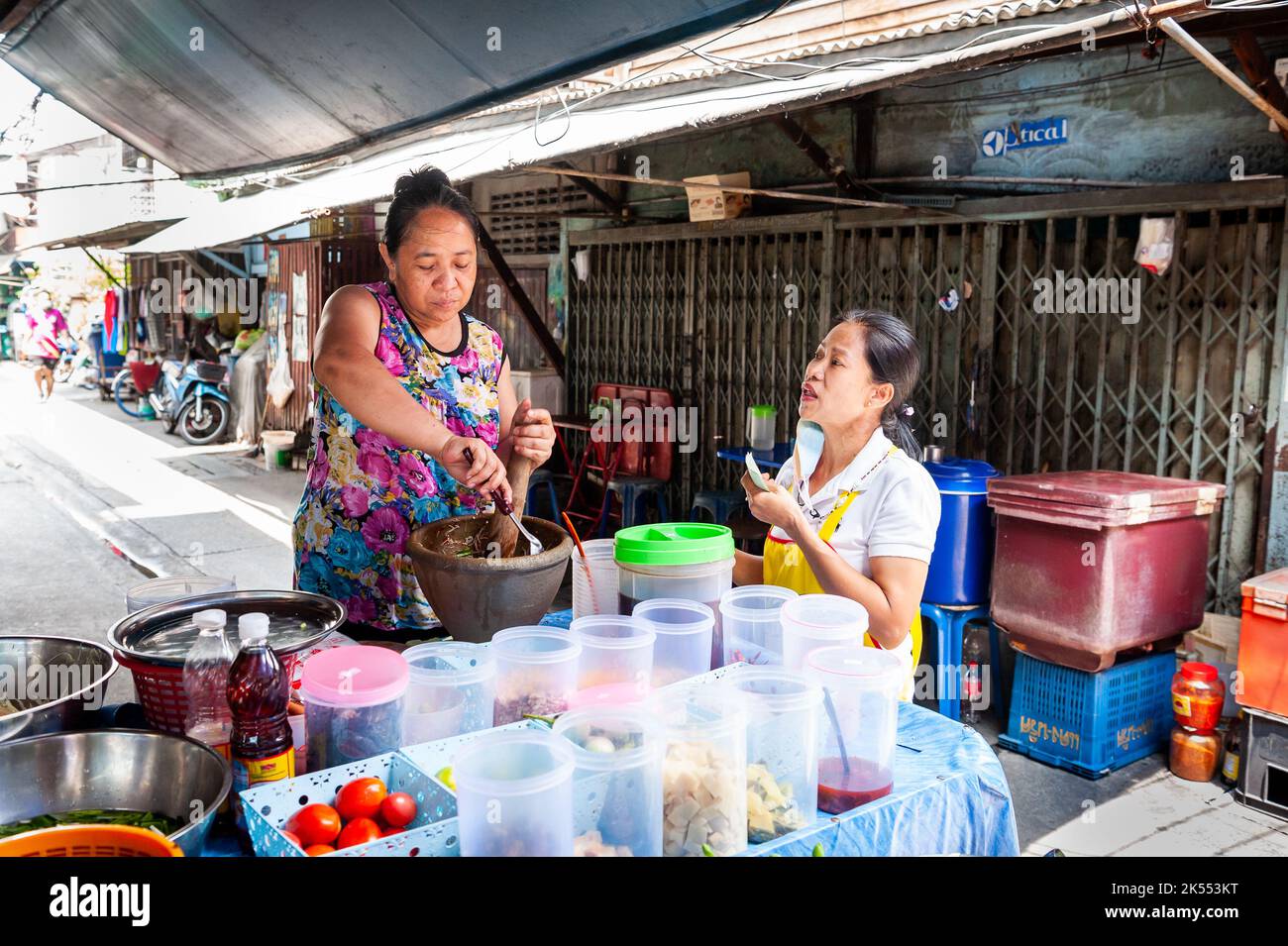 Two Thai ladies prepare food for take away in an outside market stall ...