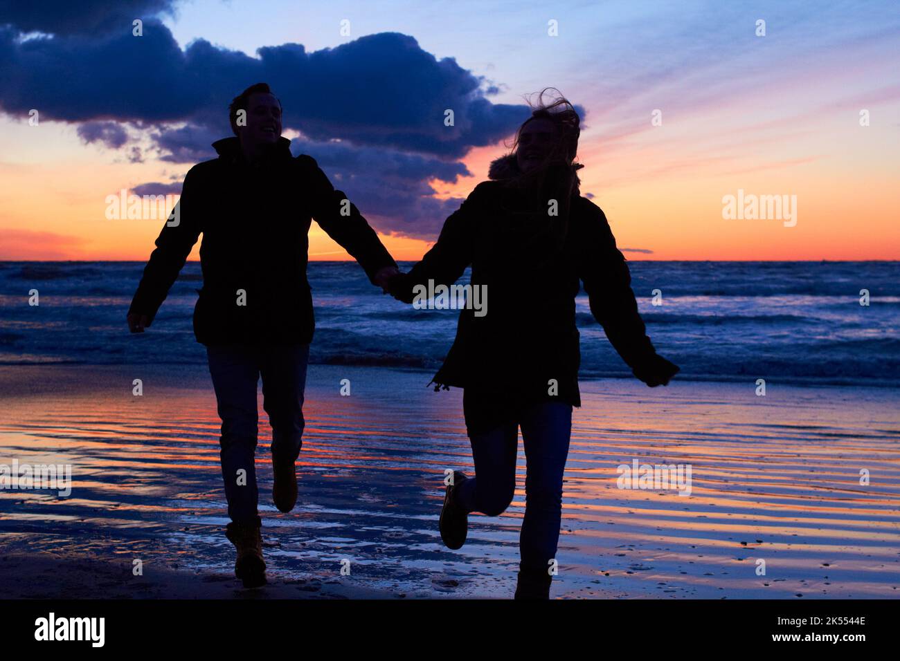 Romance at sunset. Silhouette of a couple running on the beach at ...