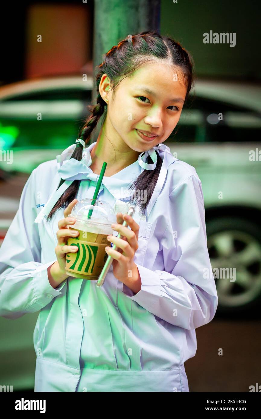 A beautiful Thai school girl poses and laughs holding her Starbucks ...