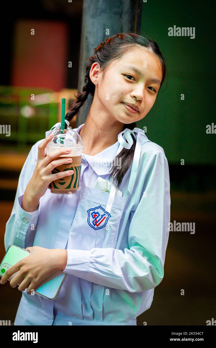 A beautiful Thai school girl poses and laughs holding her Starbucks ...