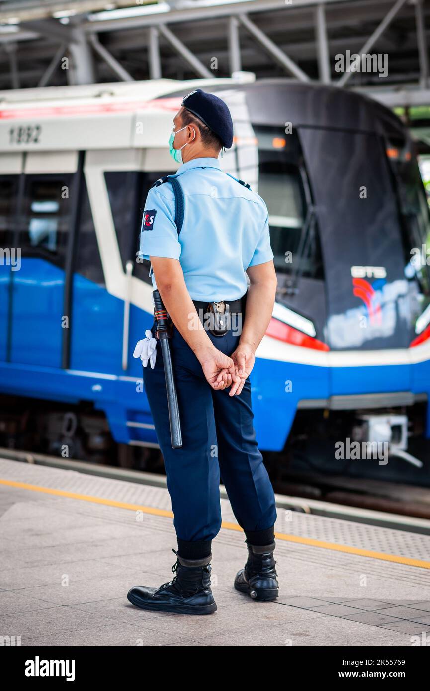 A smart Thai train guard watches the public and trains on the platform ...