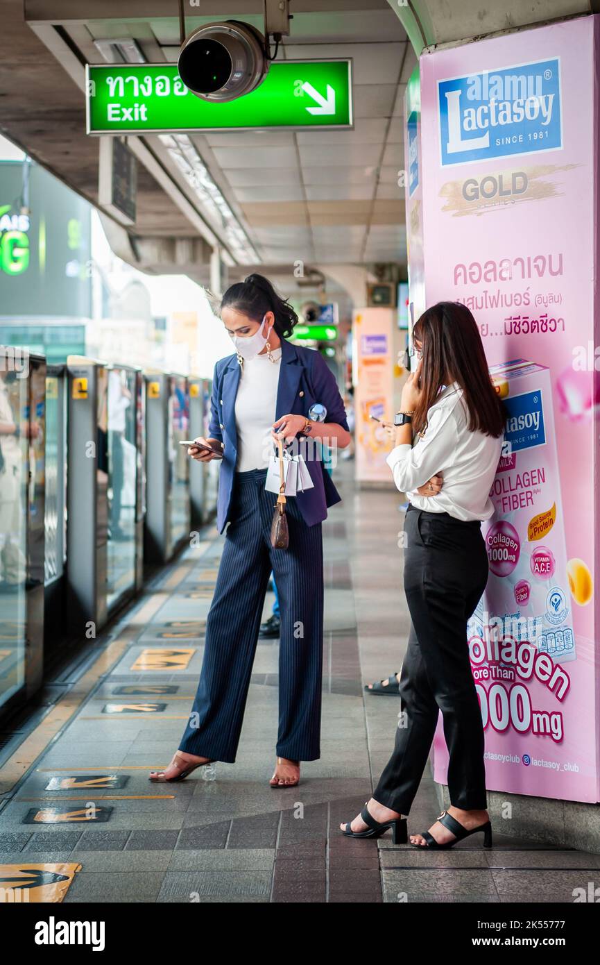 Smart and stylish Thai business women wait at Siam BTS sky train station for their train in ...