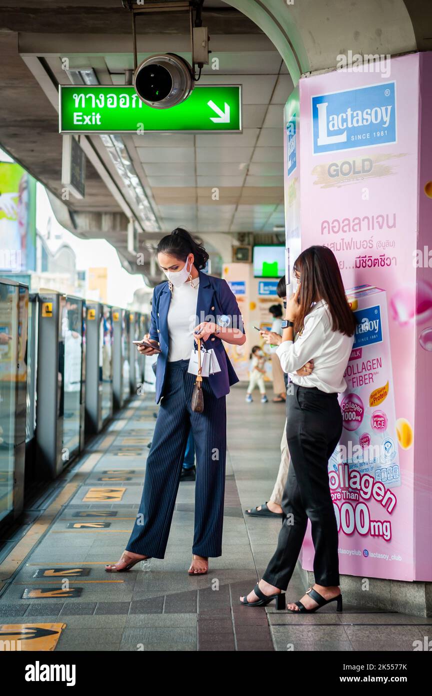 Smart and stylish Thai business women wait at Siam BTS sky train station for their train in ...