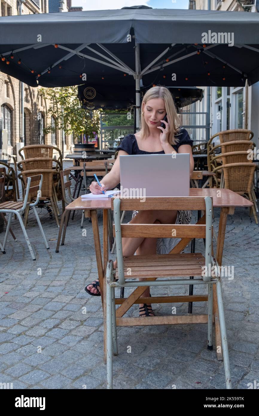 Attractive young blonde business woman using her laptop while calling ...