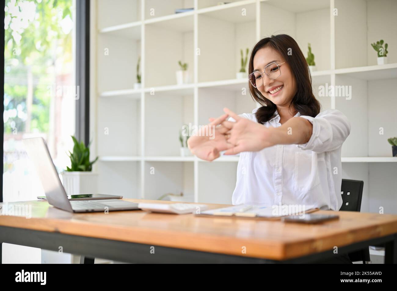 Positive and cheerful young Asian businesswoman or female office worker stretching her arms and ...