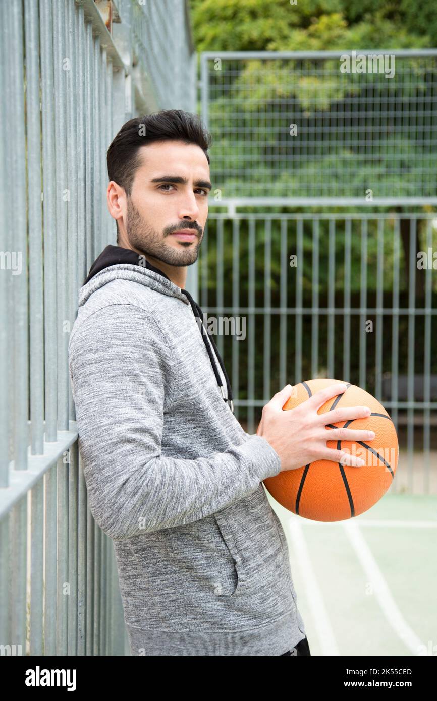 Man leaning on a public basketball court while turning to face the ...