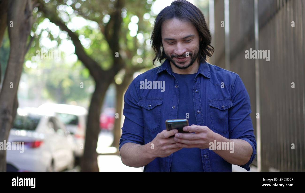 Casual Joyful South American man checking smartphone walking in city ...