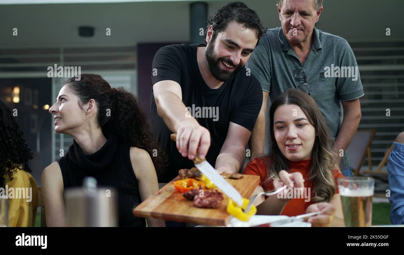 Barbecue chef serving food to friends and family at BBQ party. Happy ...