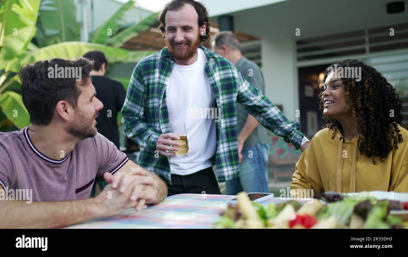 Friends conversing outdoors in home backyard barbecue. Diverse group of ...