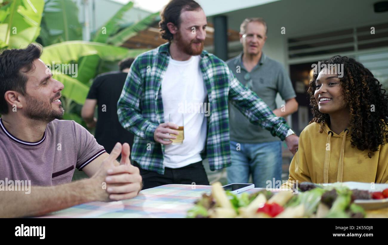 Friends conversing outdoors in home backyard barbecue. Diverse group of ...