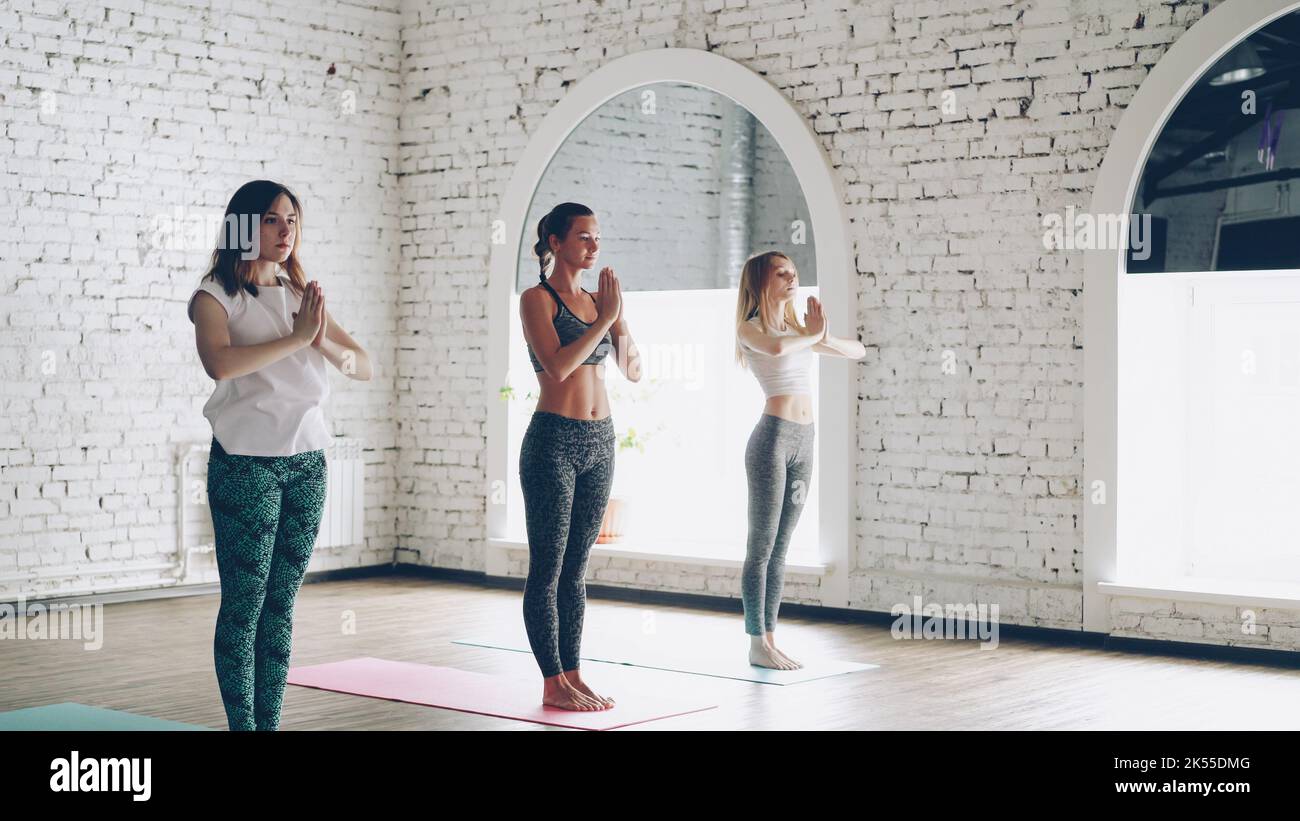 Group of three young slender women is practicing yoga doing elements of Sun Salutation Surya ...