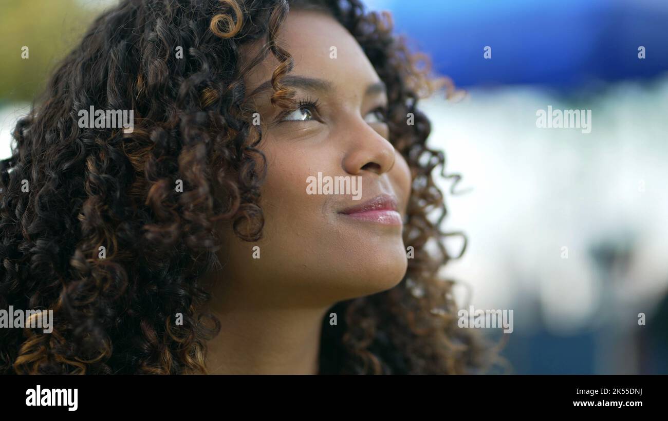 Happy young African American woman standing outdoors looks up at sky ...