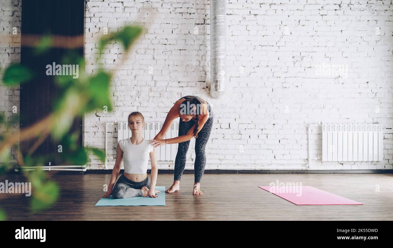 Young slim blonde is learning one-legged king pigeon pose from friendly experienced instructor ...