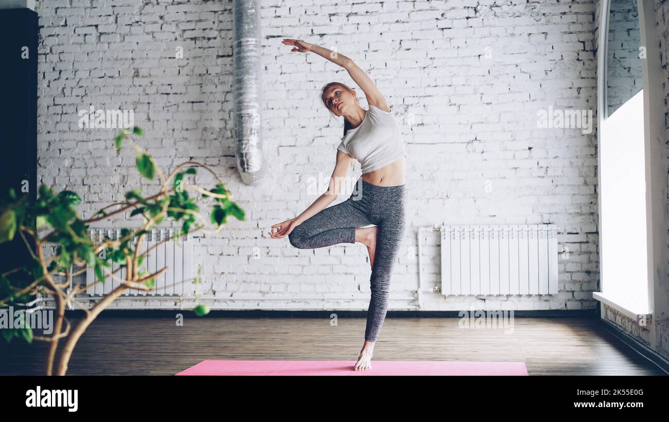 Gracious young woman is doing yoga practicing tree pose Vriksasana ...