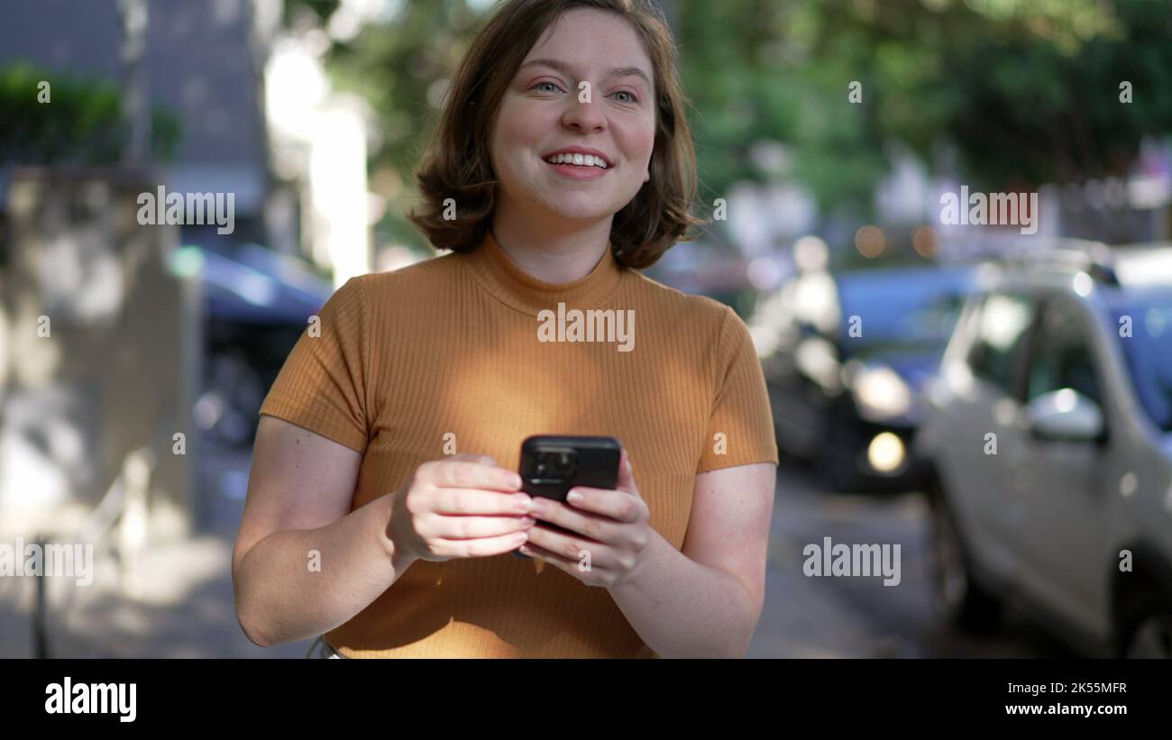 Person checking phone while walking outside in city street. Young woman looking at cellphone in ...