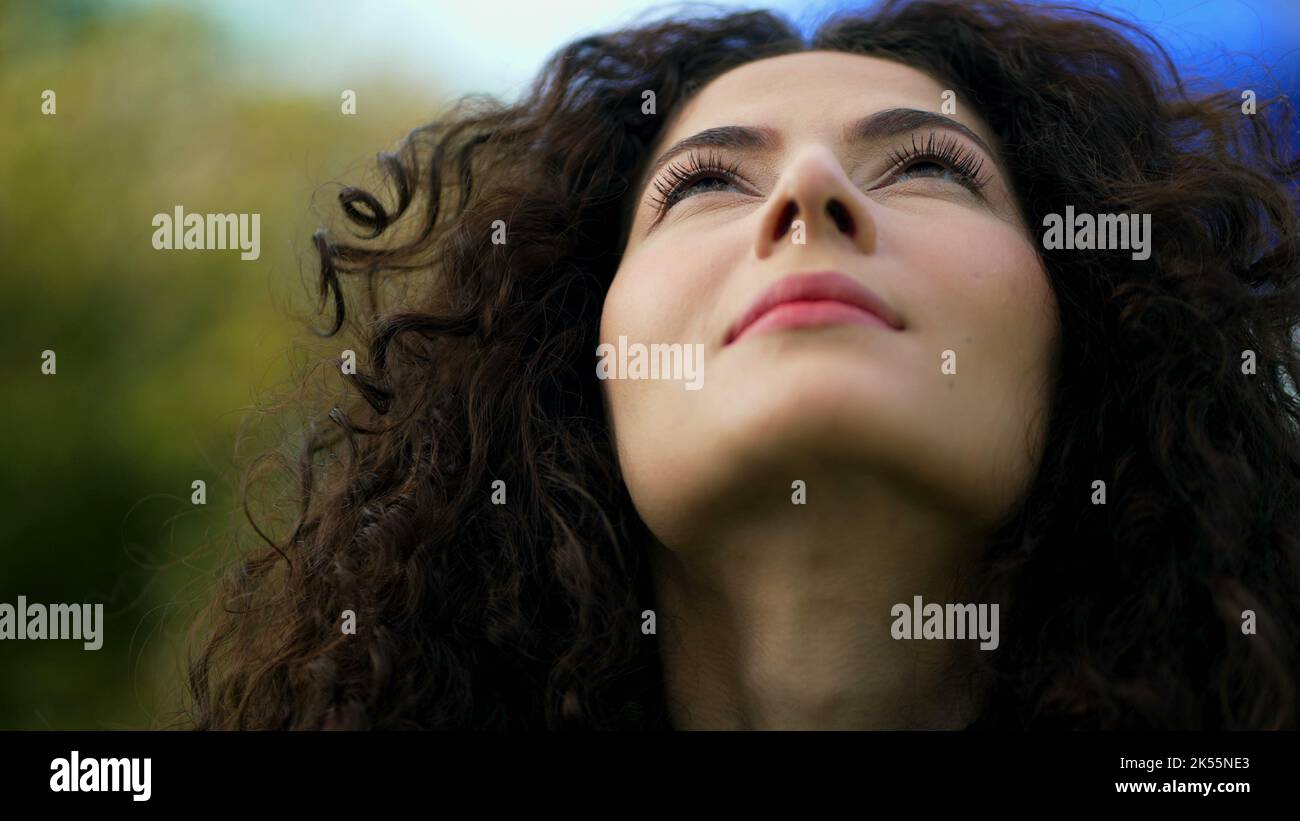 One hopeful hispanic young woman looking up at sky with FAITH ...