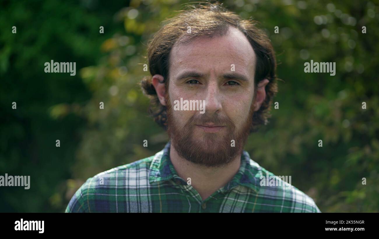 Portrait of a casual serious man looking at camera standing outdoors ...