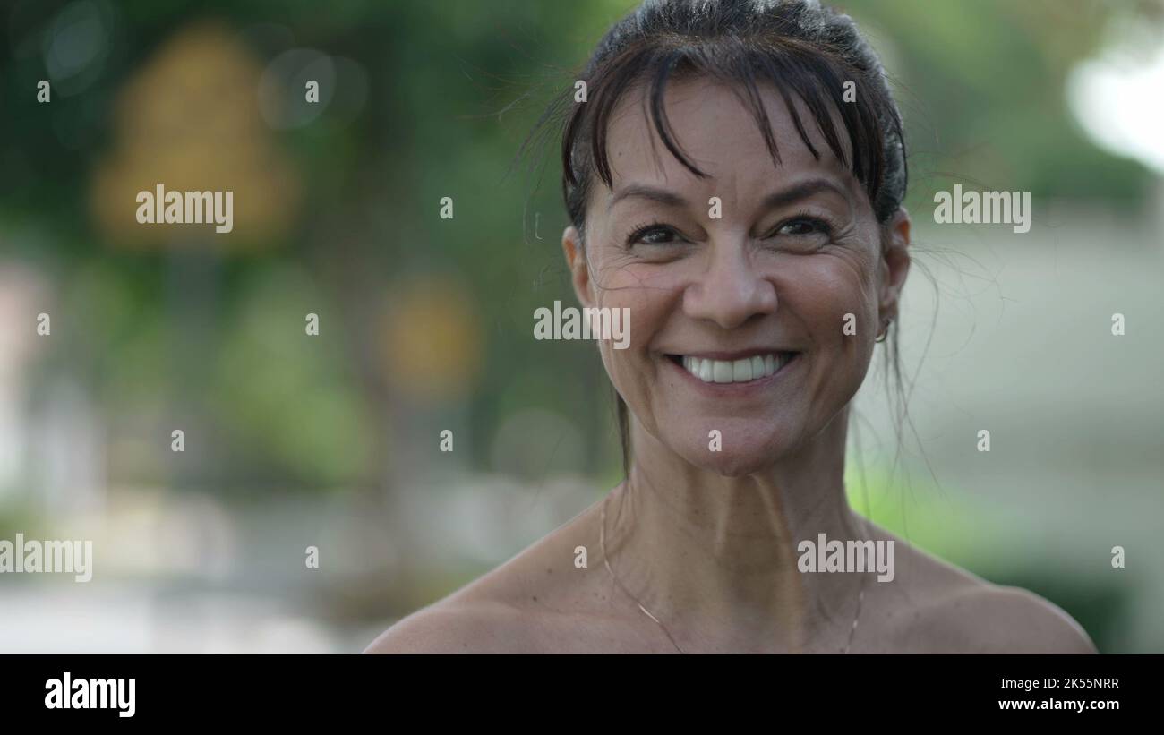 Portrait of a happy middle aged woman smiling at camera standing outdoors. One older female ...