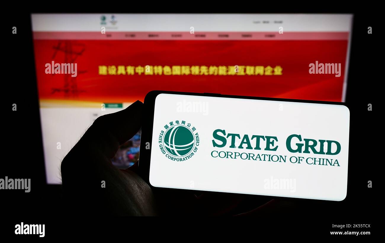 Person holding cellphone with logo of company State Grid Corporation of ...