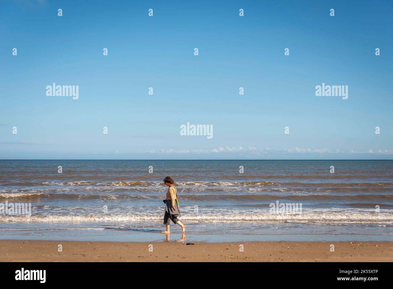 Middle aged woman walking along the tide line at Fraisthorpe Beach ...