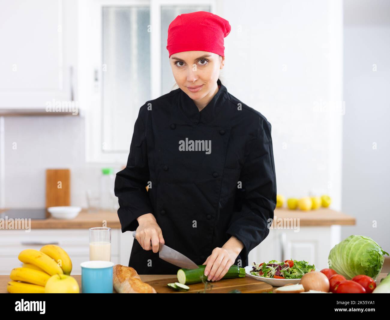 Smiling female chef in black uniform preparing vegetable salad in ...