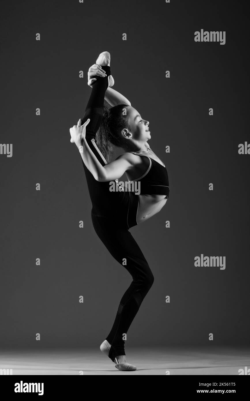 A young flexible girl gymnast in a tracksuit does gymnastic stretching ...