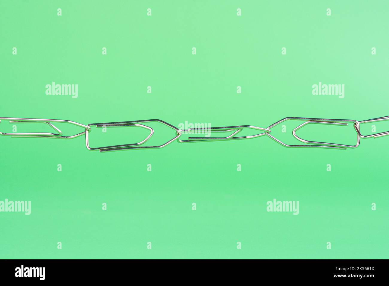 Paper clips connected to each other on green background Stock Photo - Alamy