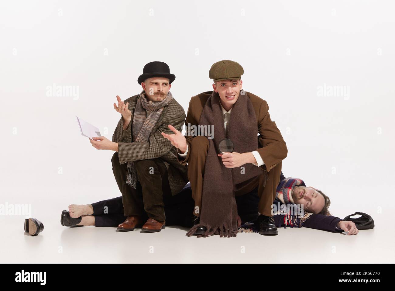 Portrait of two emotive man in image of detectives sitting on lying man ...