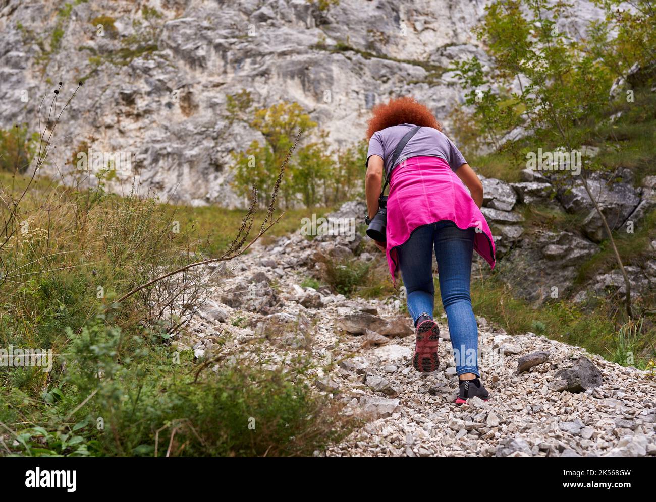 Tourist woman with curly hair with camera hiking on a steep trail in ...