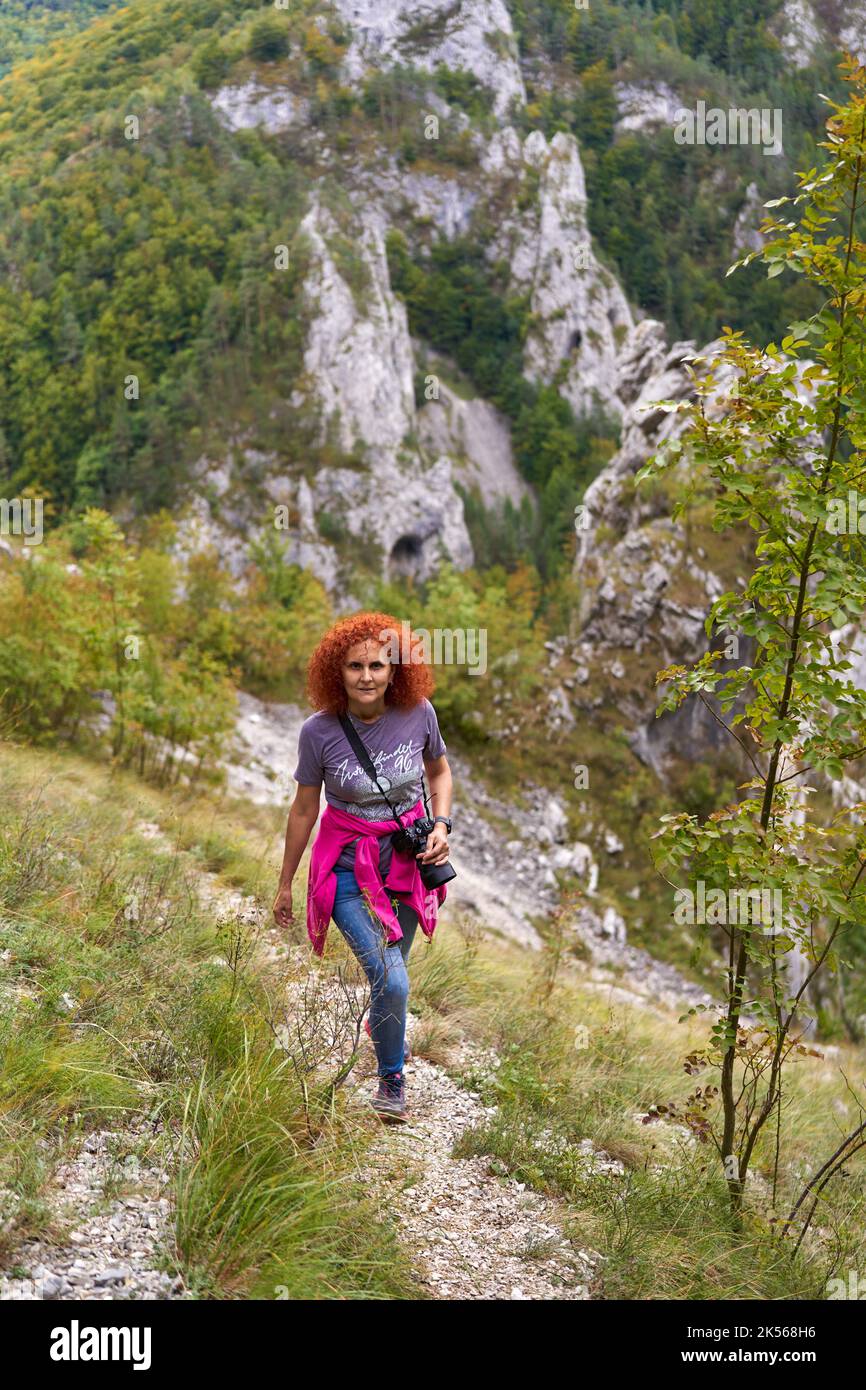Tourist woman with curly hair with camera hiking on a steep trail in ...