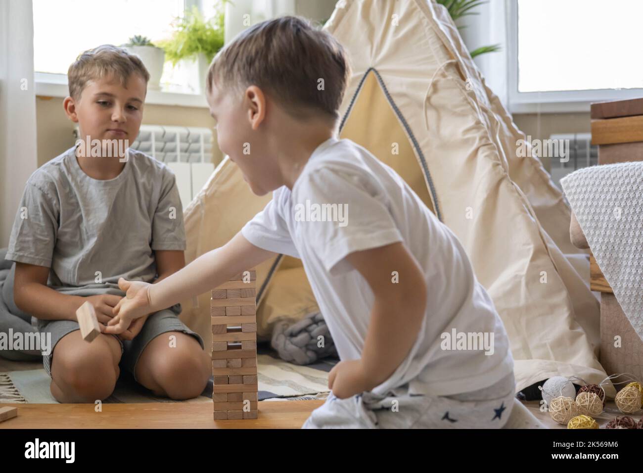 Two male children playing Jenga hardwood bricks tower construction ...