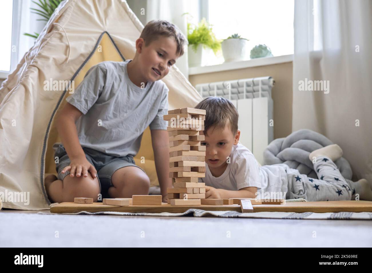 Two male children playing Jenga hardwood bricks tower construction ...