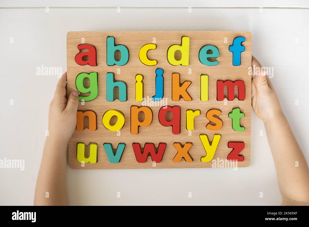Childish hands holding alphabet wooden board with colored font letters ...