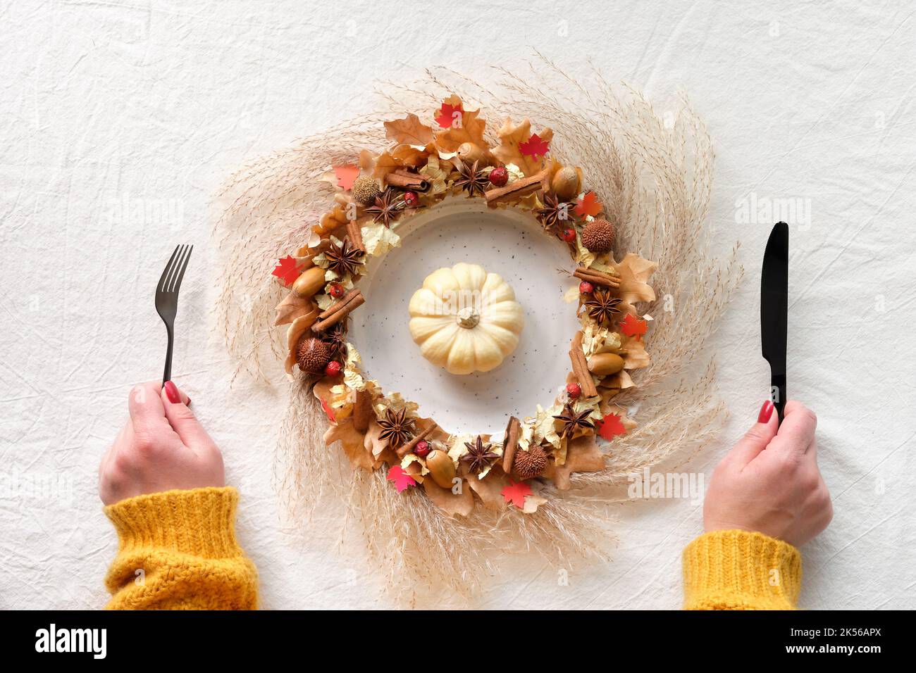 Autumn wreath and white pumpkin on a plate. Hands with kitchen utensils ...