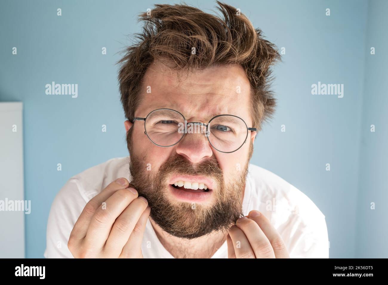 Shaggy man touches his beard, he is perplexed, dissatisfied and annoyed ...