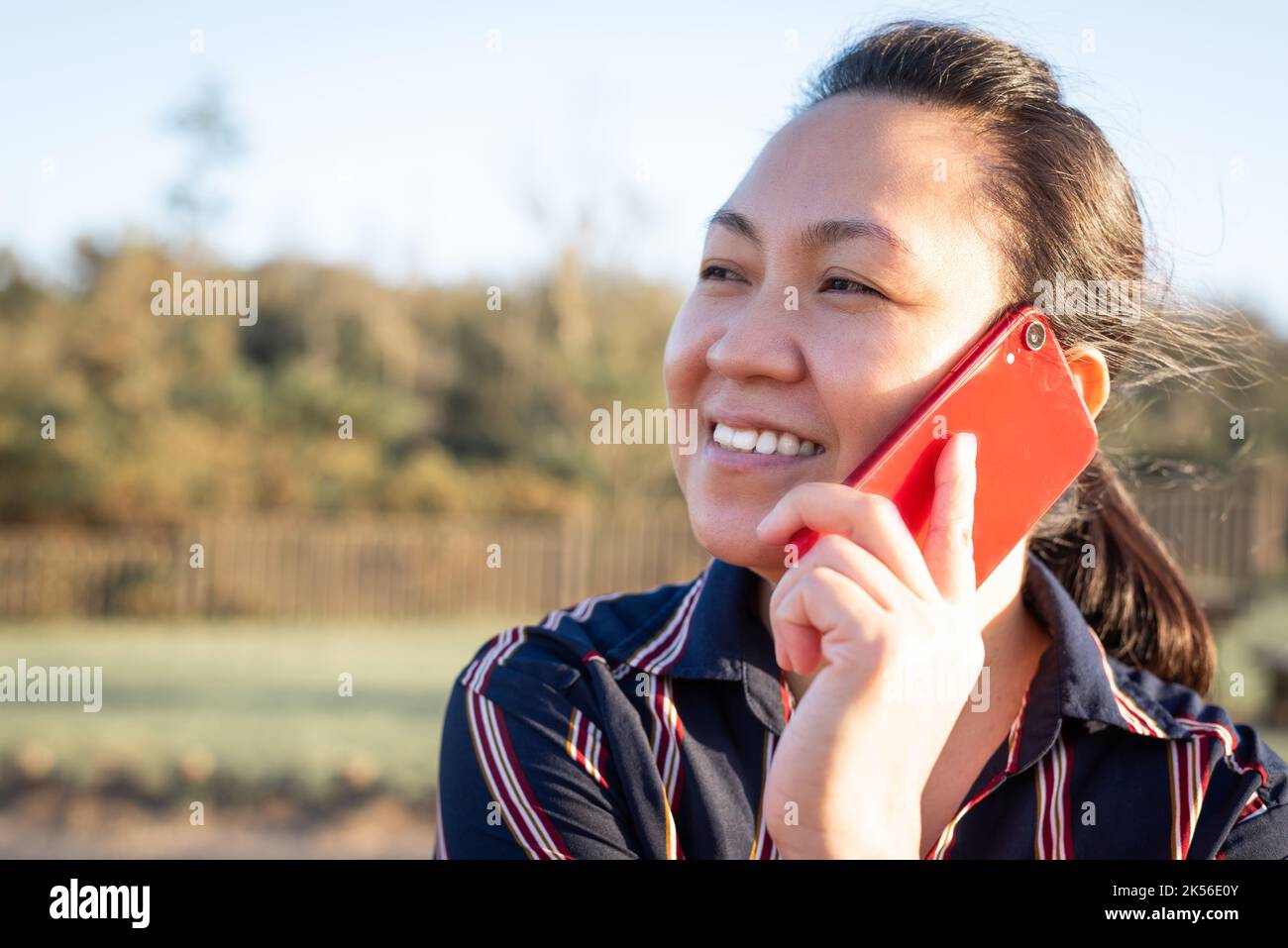 An Asian Filipino woman happily talks on the phone during sunset. Close ...