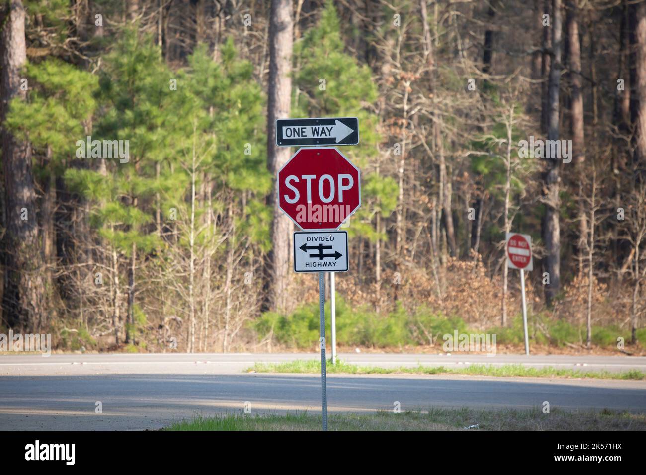 One way, stop sign, and divided highway signs with a forest in the ...