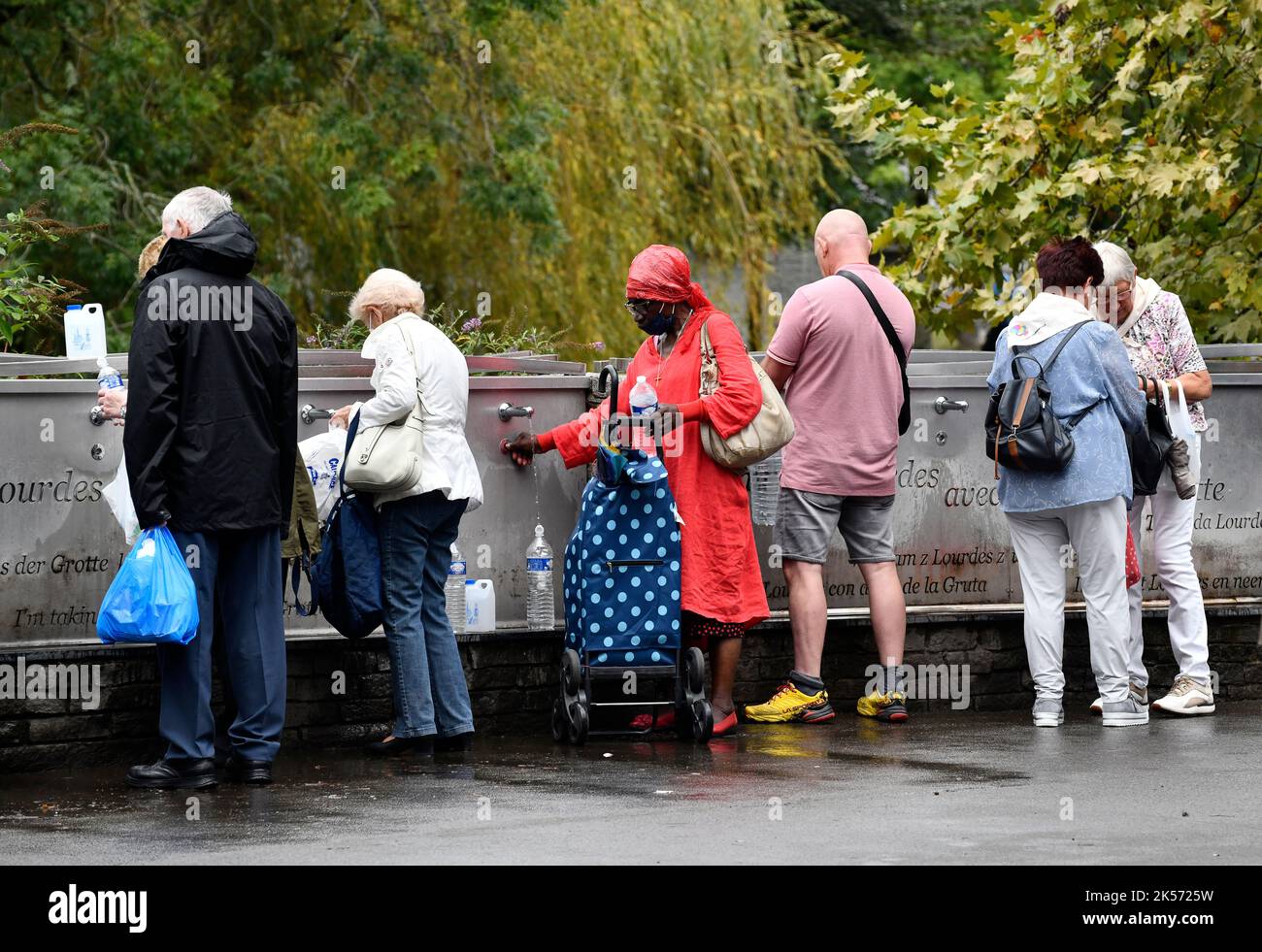 Lourdes, Hautes-Pyrénées, France. Christian pilgrims collecting Lourdes ...