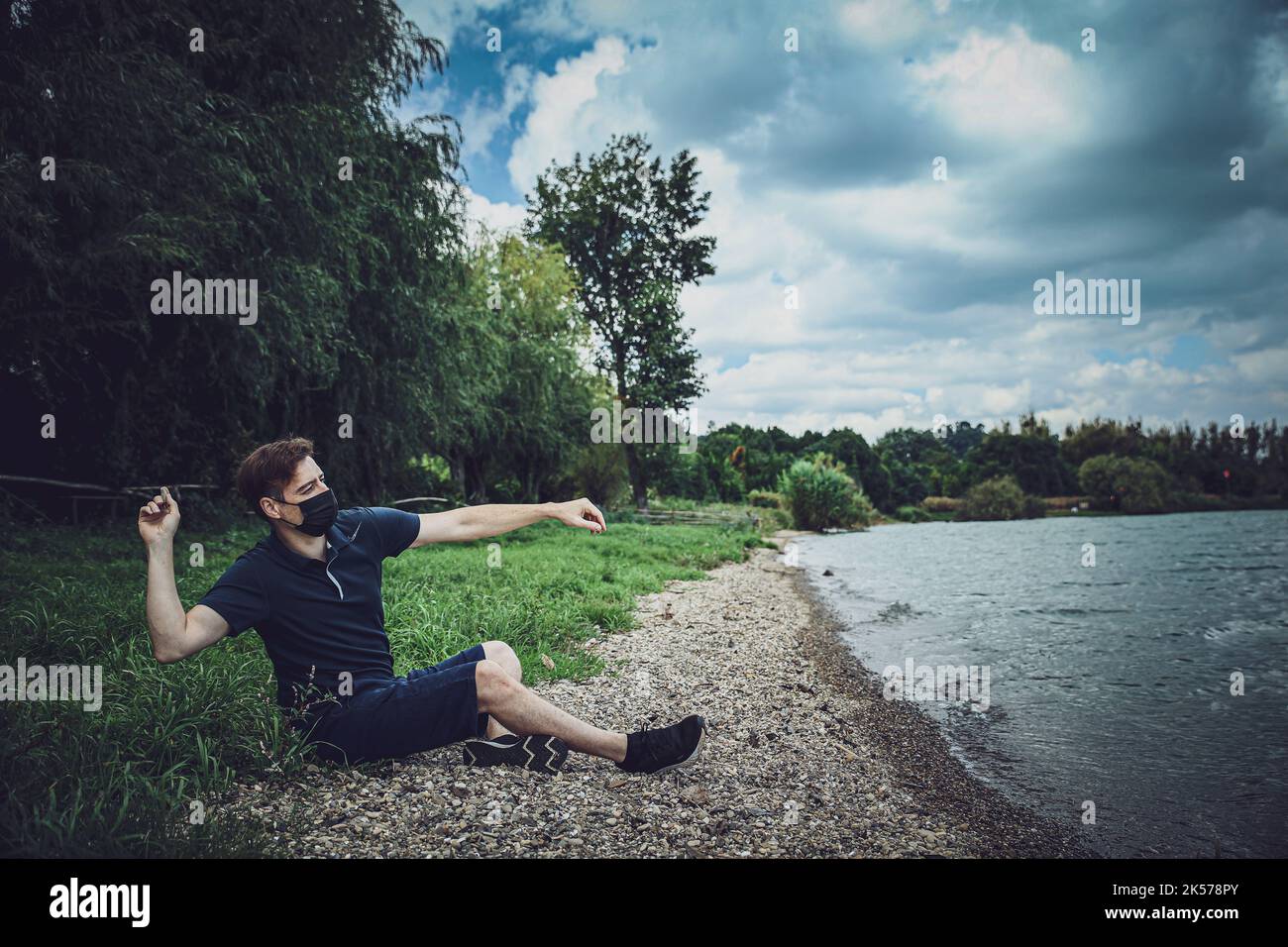 Masked guy is sitting and throwing a stone to lake Stock Photo - Alamy