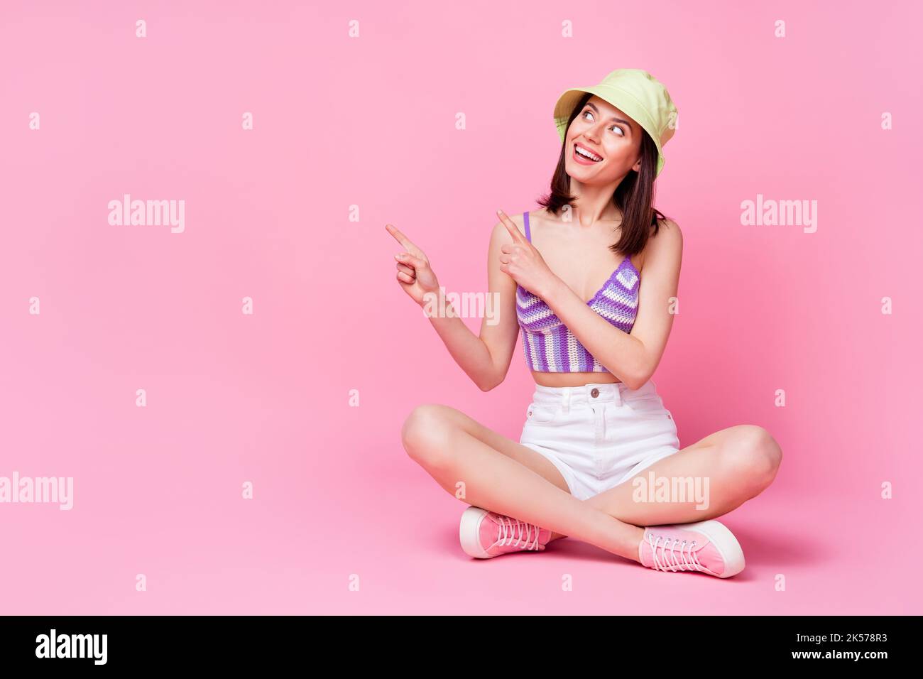 Full size photo of cheerful pretty lady sit floor look indicate fingers ...