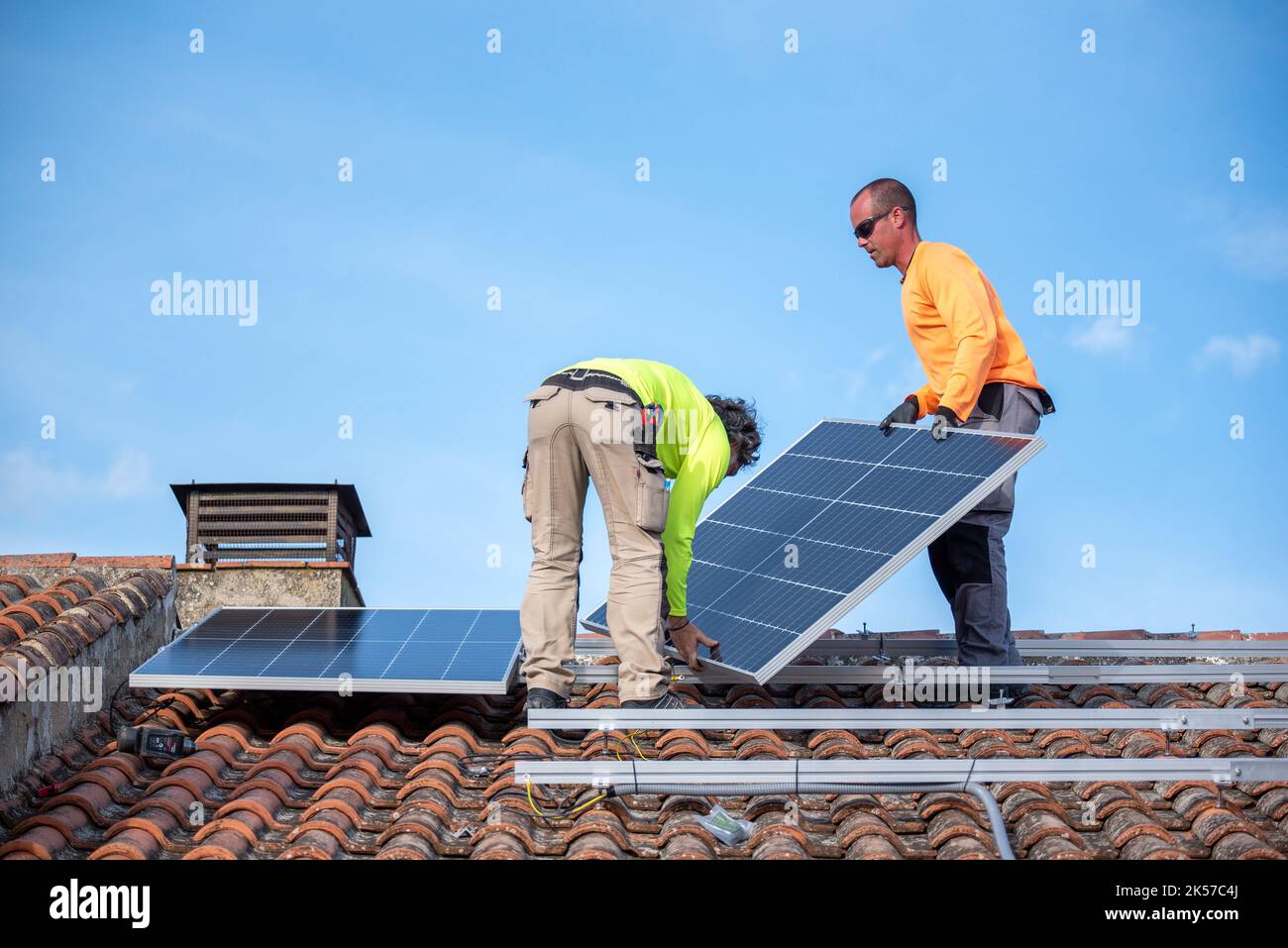 Roof with two people installing solar panels and a blue sky with white ...