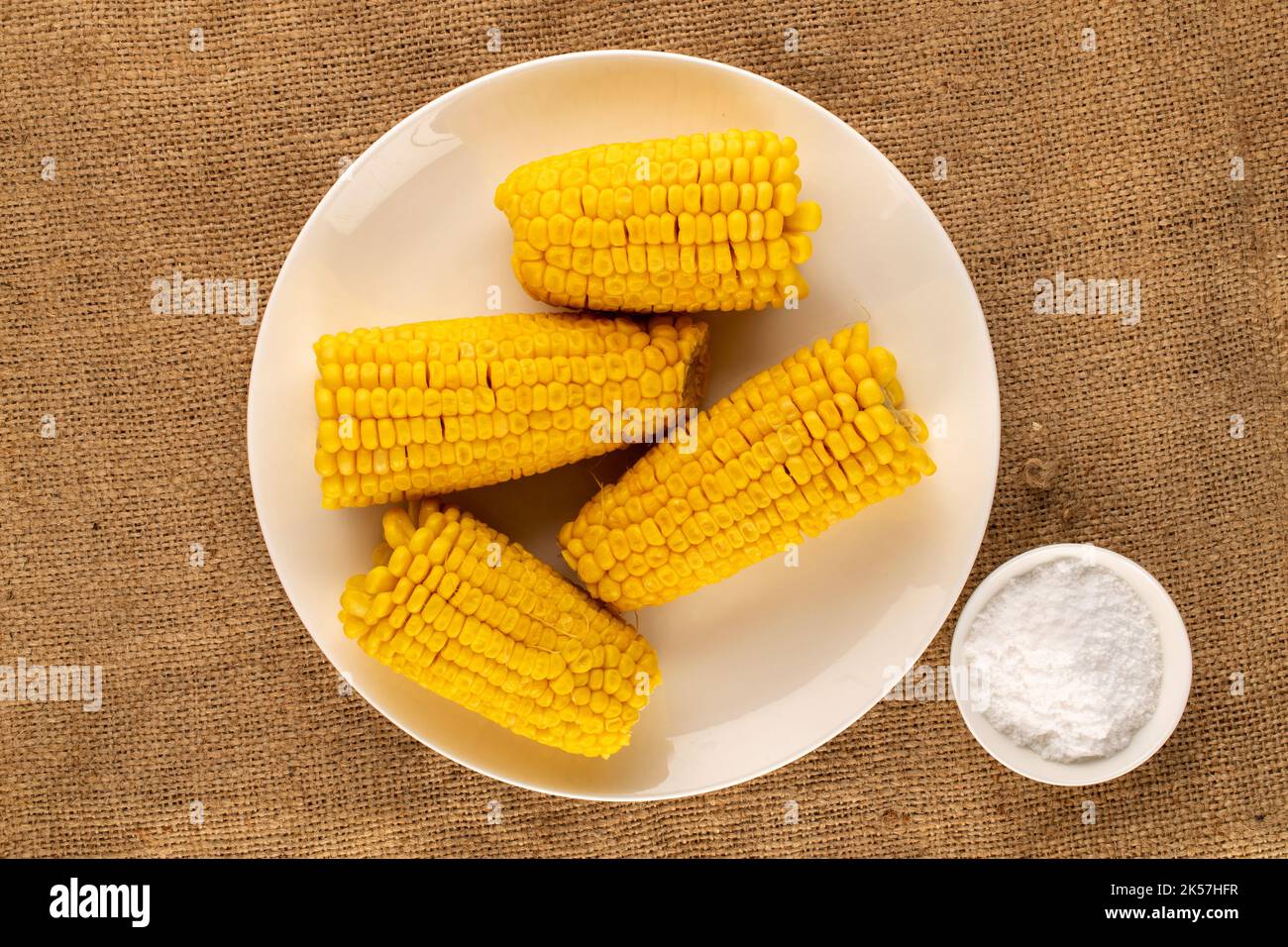 Several fragrant boiled corn with white plate and salt on jute cloth ...