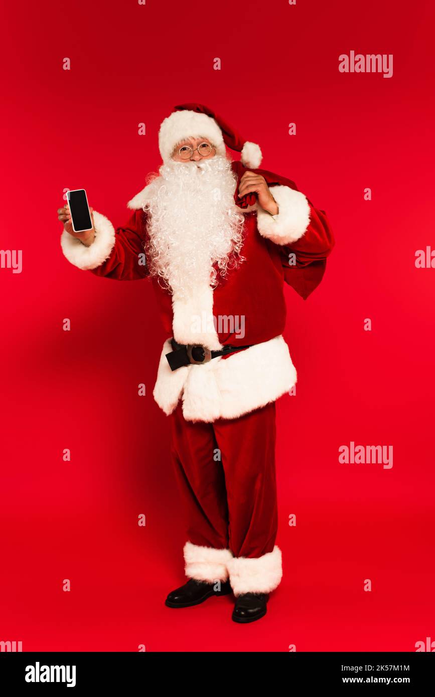 Santa claus in costume holding sack and cellphone with blank screen on ...