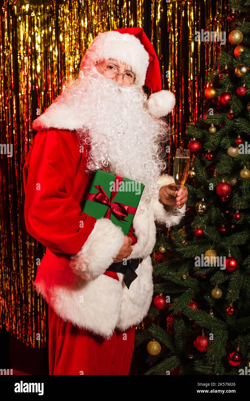 Santa claus in eyeglasses holding champagne and present near christmas ...